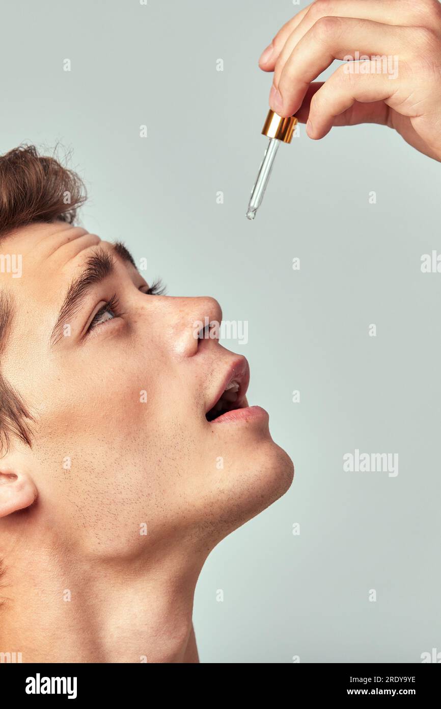 Young smiling brown-haired guy applies a beauty serum on his face ...