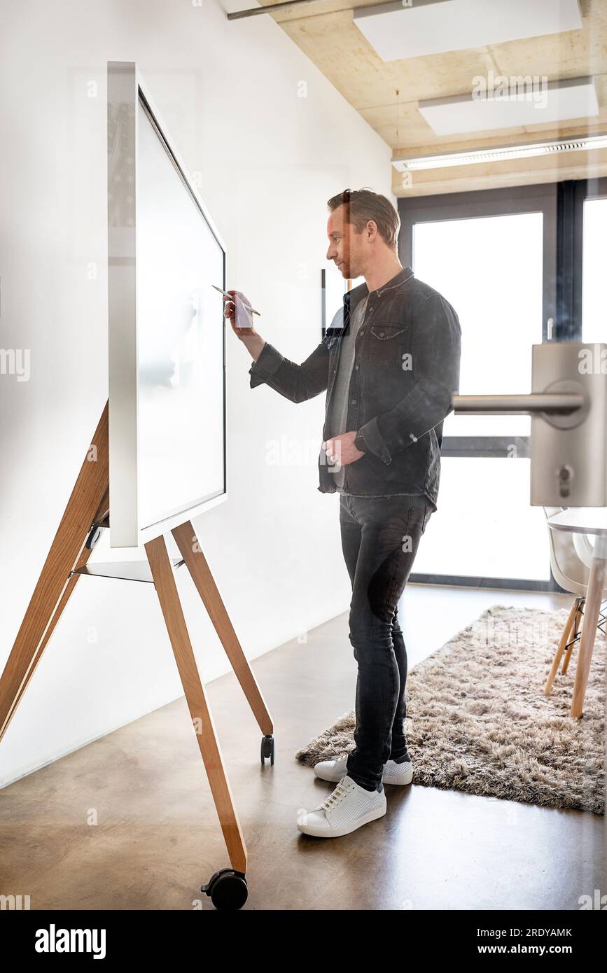 Businessman with digitized pen writing on interactive whiteboard seen ...