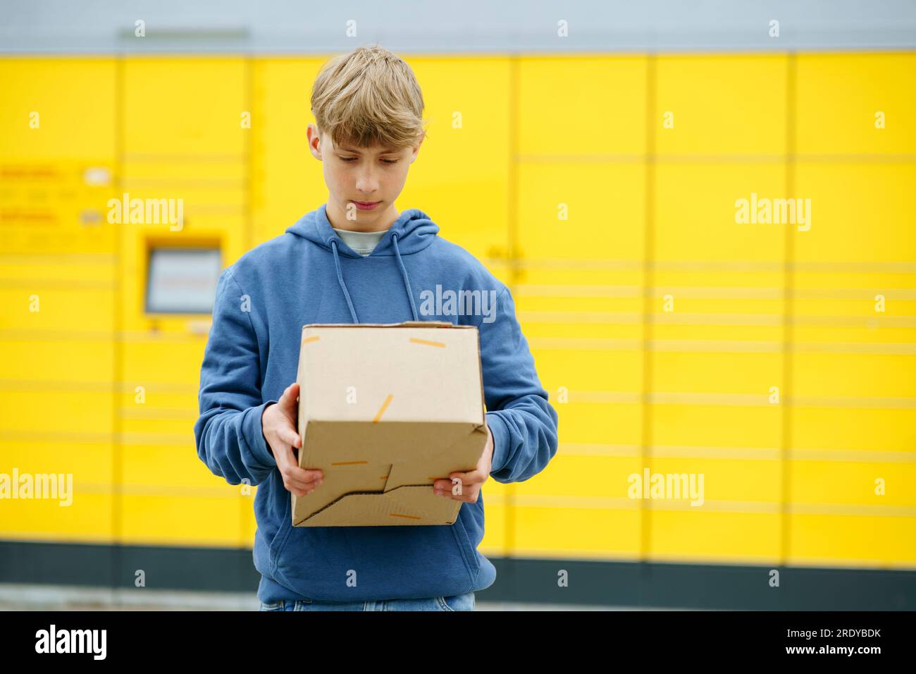Boy examining package standing in front of yellow parcel locker Stock ...