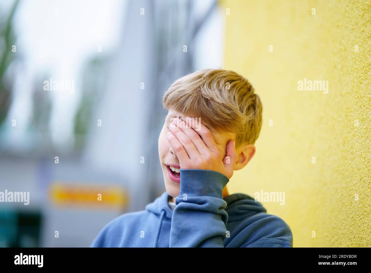 Blond boy covering face with hand in front of yellow wall Stock Photo ...