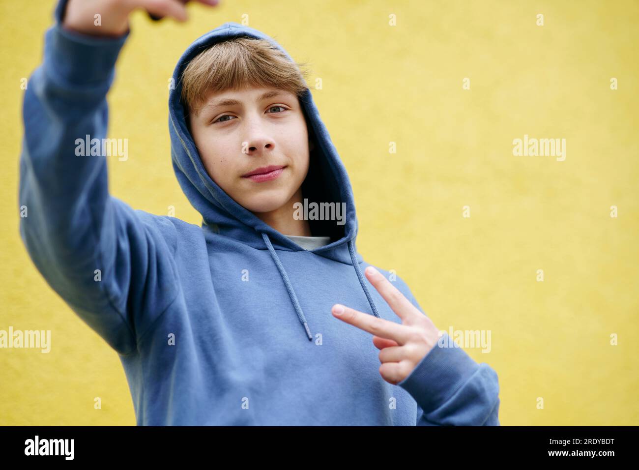 Smiling boy showing peace sign gesture and taking selfie in front of ...