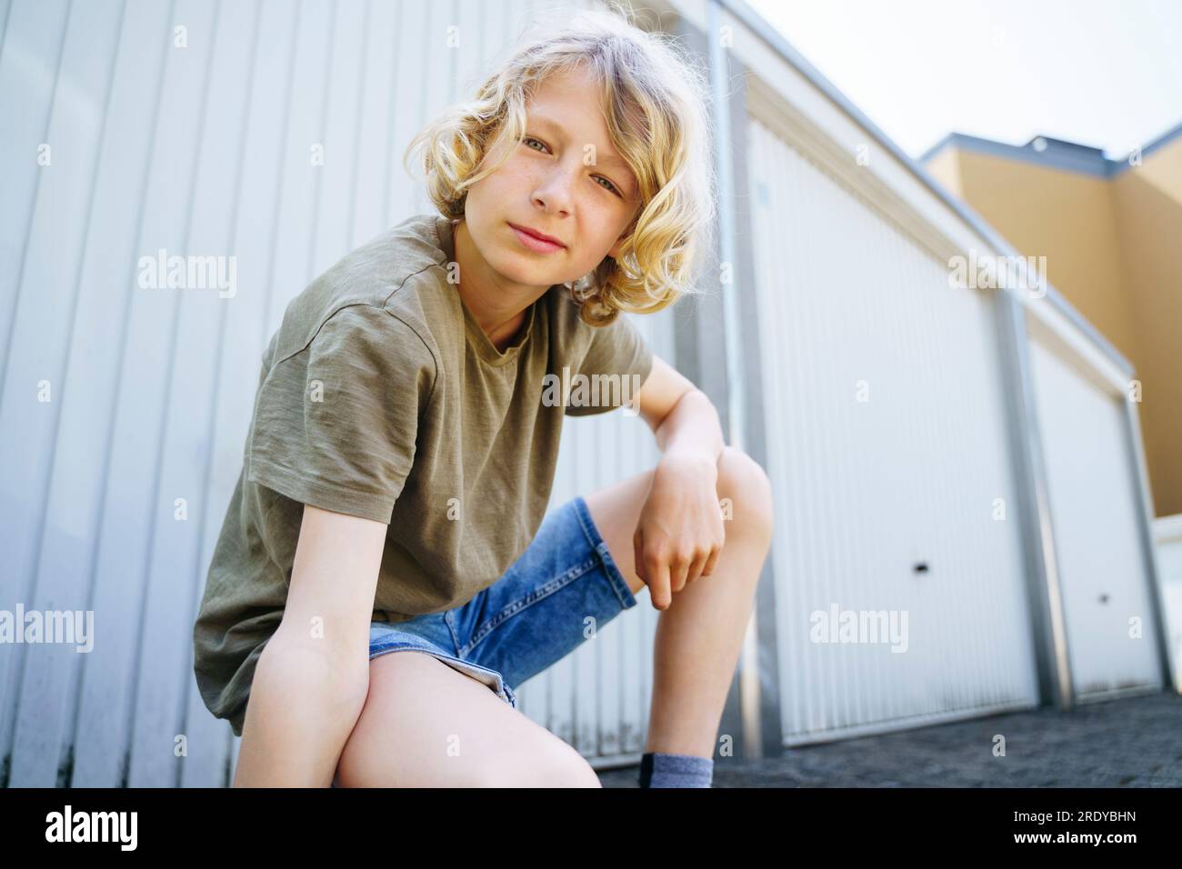 Boy with blond hair crouching outside garage Stock Photo - Alamy