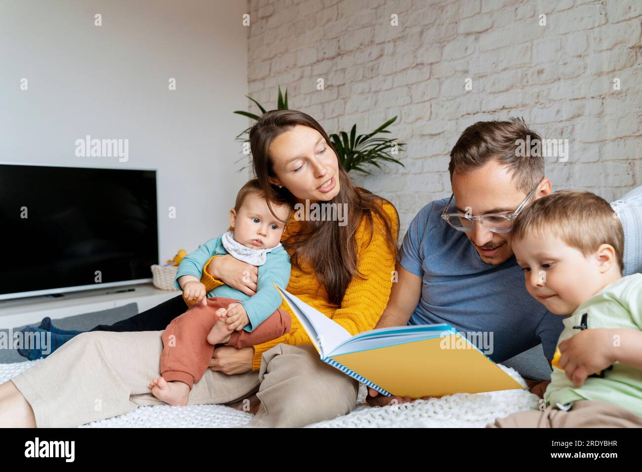 Parents reading book for children on couch at home Stock Photo - Alamy