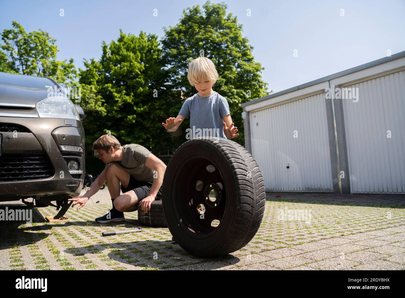 Boy helping father changing car tire in yard Stock Photo - Alamy
