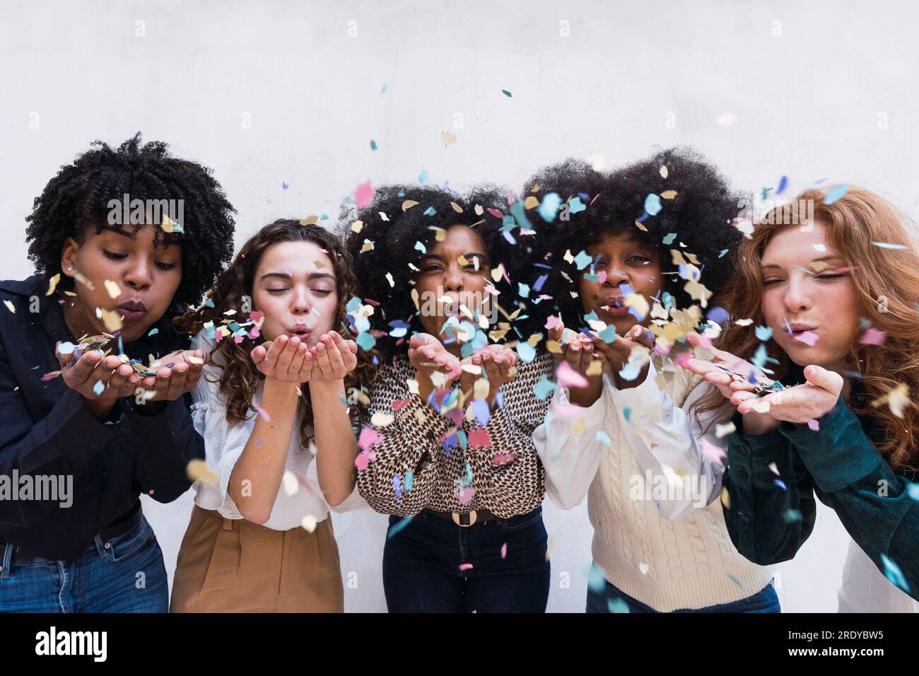 Happy businesswomen blowing confetti in front of wall Stock Photo - Alamy