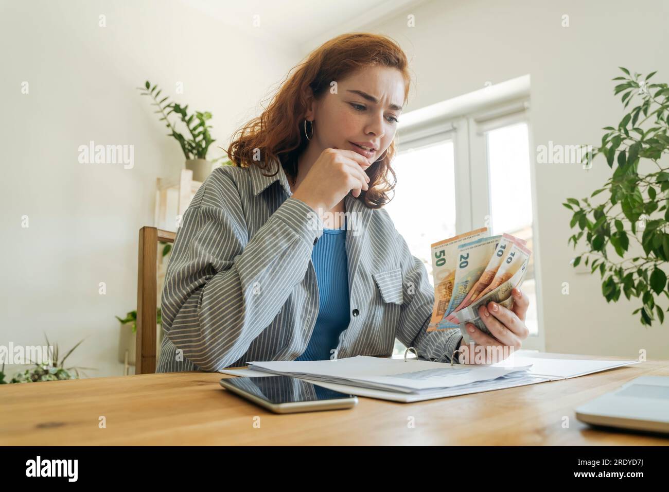 Confused young woman calculating financial bills and counting currency ...