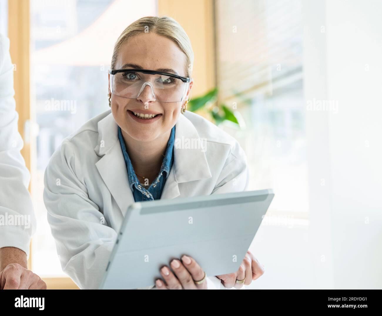 Smiling scientist wearing lab coat holding tablet PC in laboratory ...