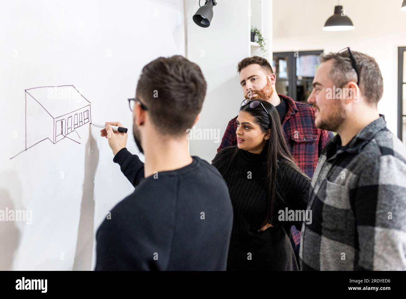 Architect drawing on white board and explaining to colleagues in office ...