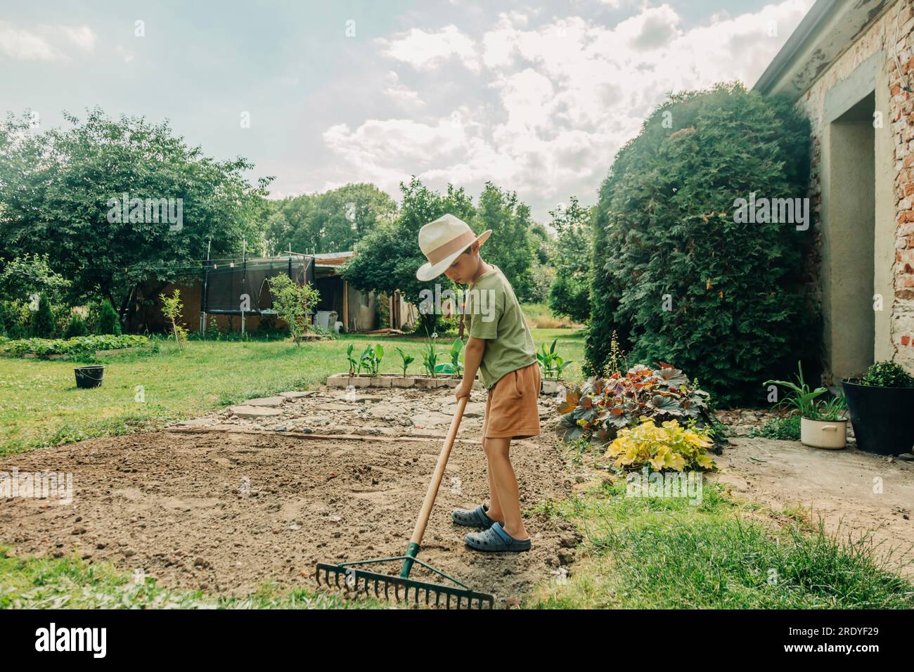 Boy raking flower bed in summer wearing straw hat Stock Photo - Alamy