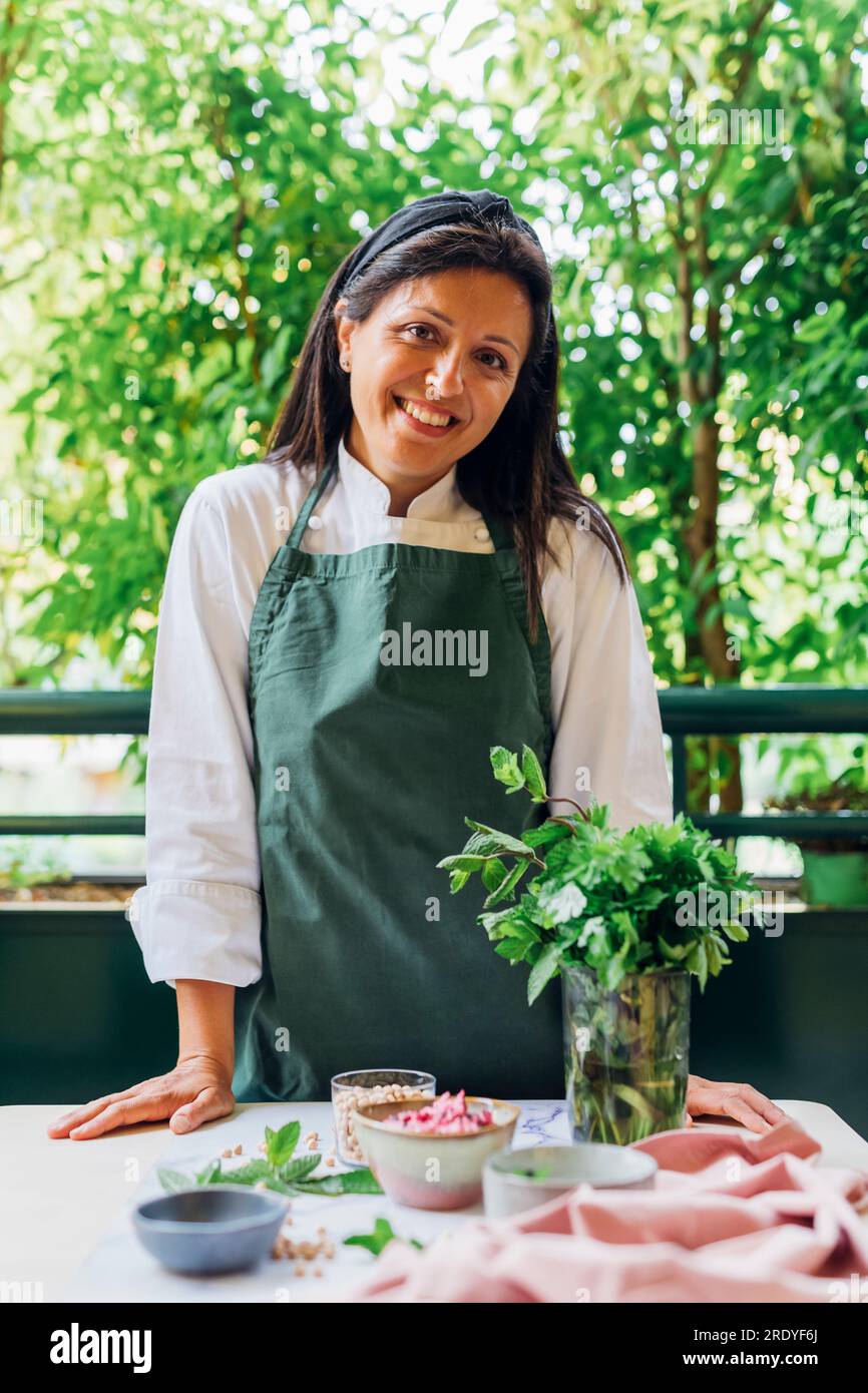 Smiling chef wearing apron standing near table in balcony Stock Photo ...