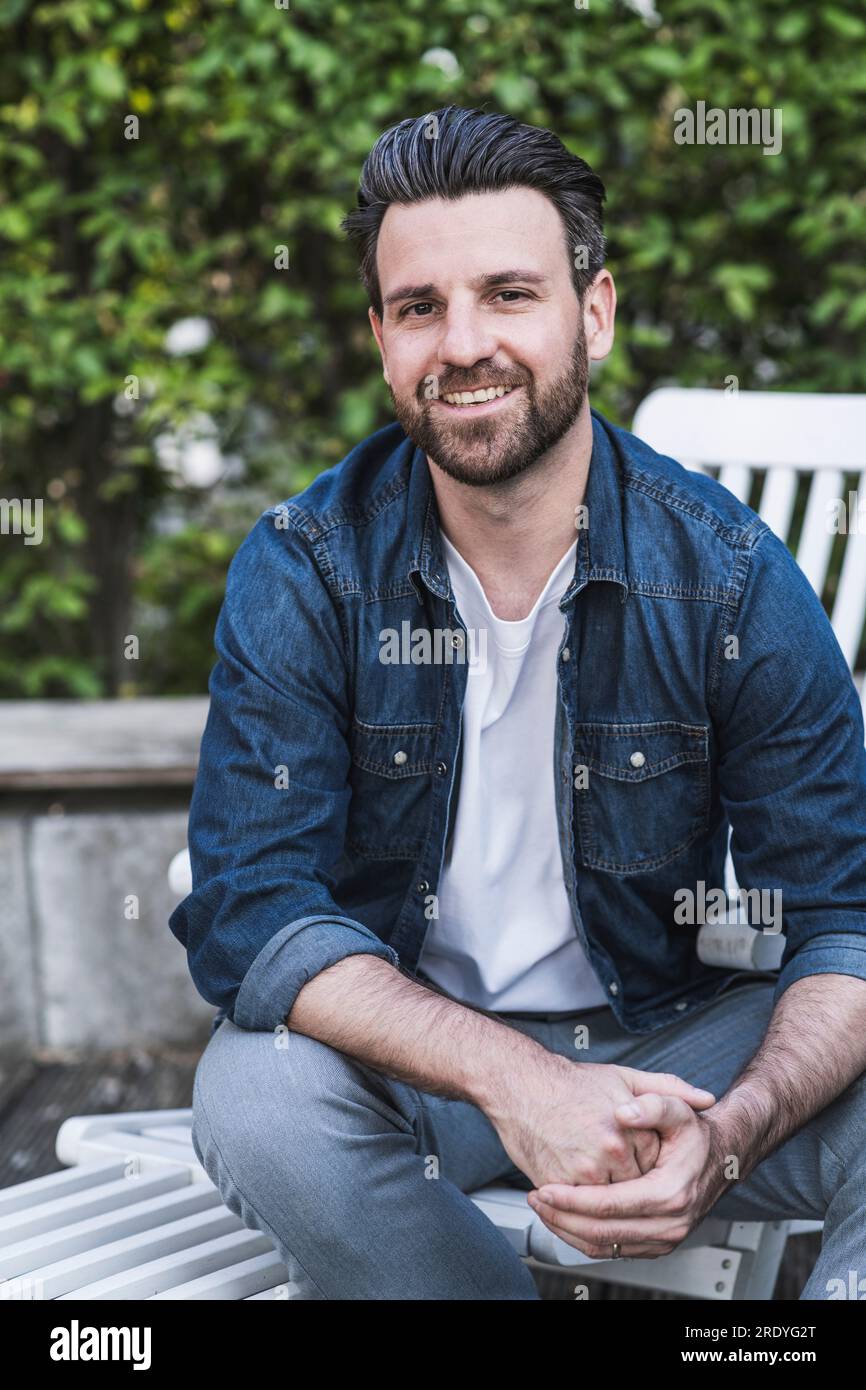 Happy man sitting on chair in front of plants Stock Photo - Alamy