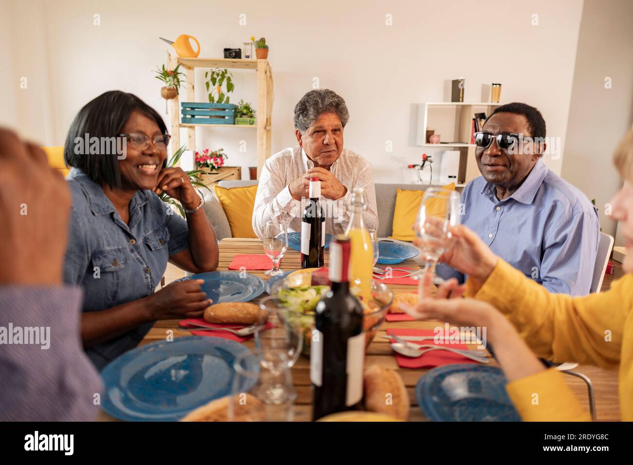 Multi-cultural senior friends having dinner at dining table in home ...