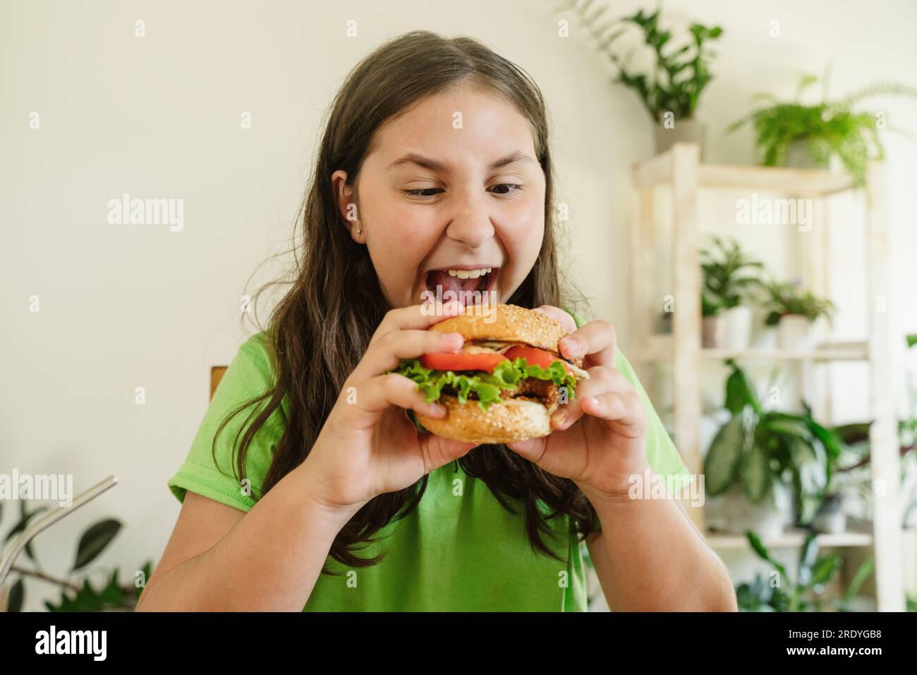 Girl holding burger with open mouth at home Stock Photo - Alamy