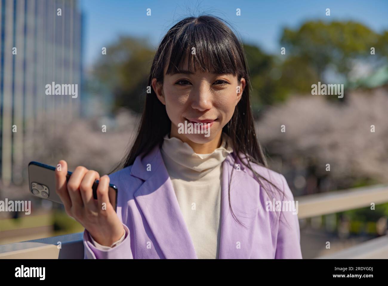 A portrait of Japanese woman with smartphone behind cherry blossom bust ...
