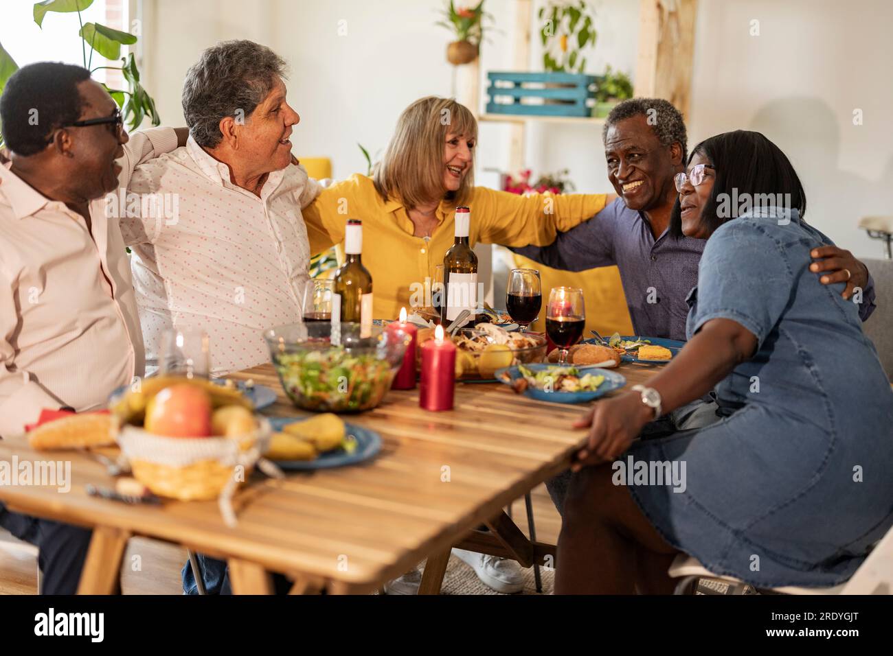 Happy multi-cultural senior friends sitting with arms around at dining ...
