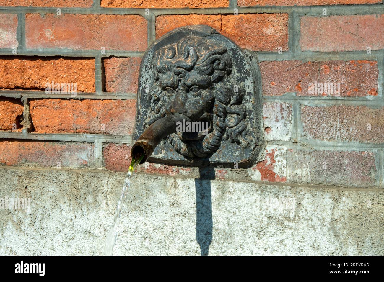 Stone lion fountain with flowing water against a brick wall in daylight ...