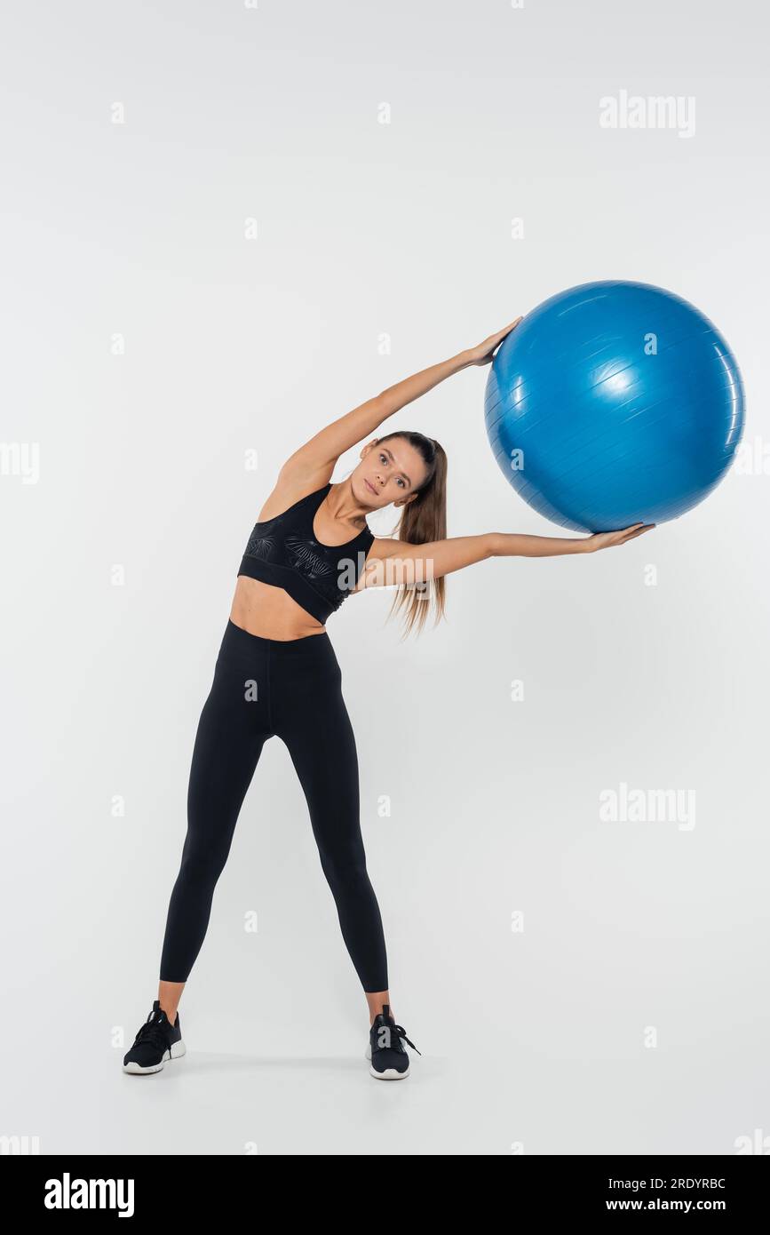 woman exercising with stability ball and standing on white background ...