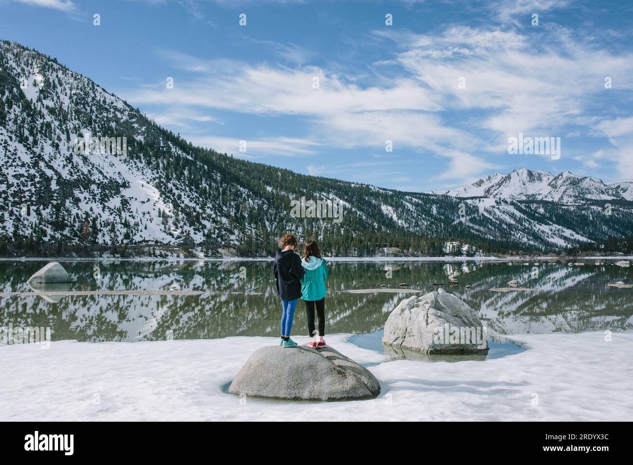 The backs of two girls atop a rock in a partially frozen lake Stock ...