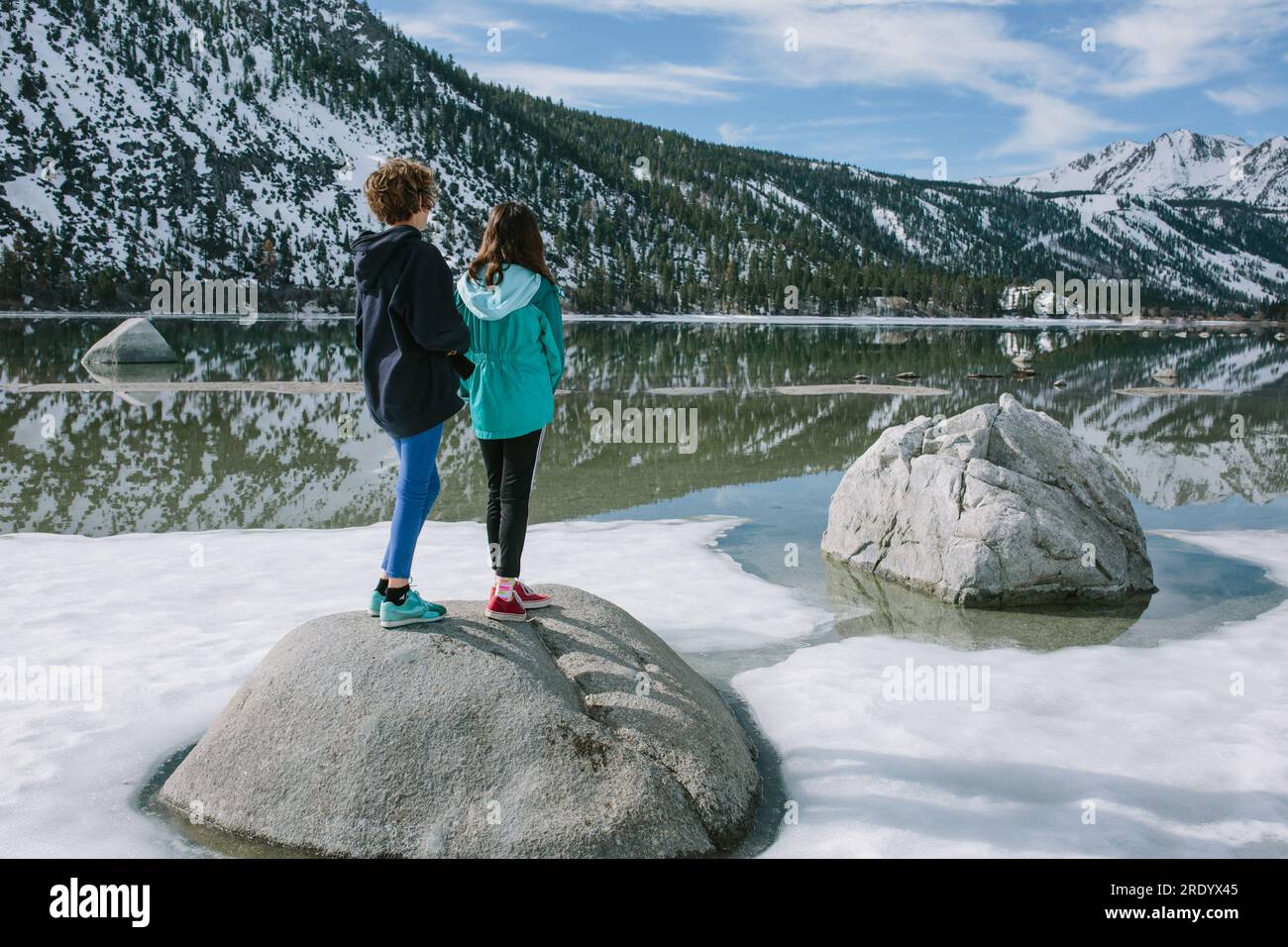 The back of two girls looking at the view while atop of rock in lake ...