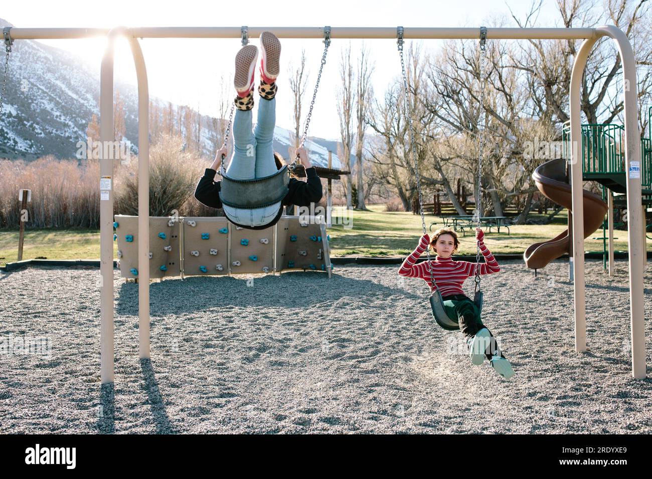 Girl Up High On The Swings With Sister By Her Side Swinging Low Stock