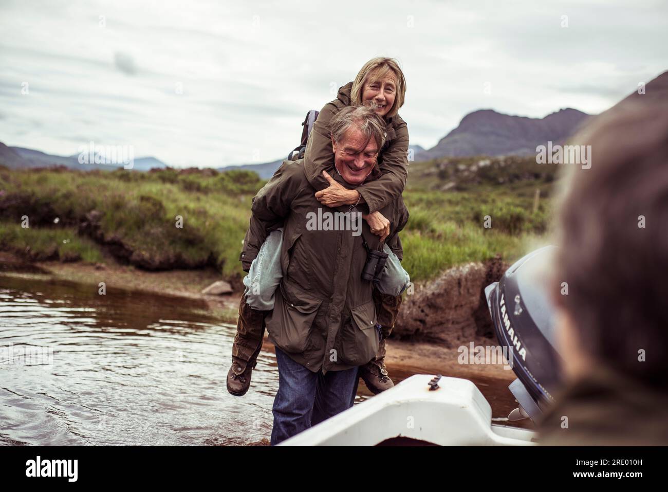 retired couple piggy back carry across remote mountain fishing river ...