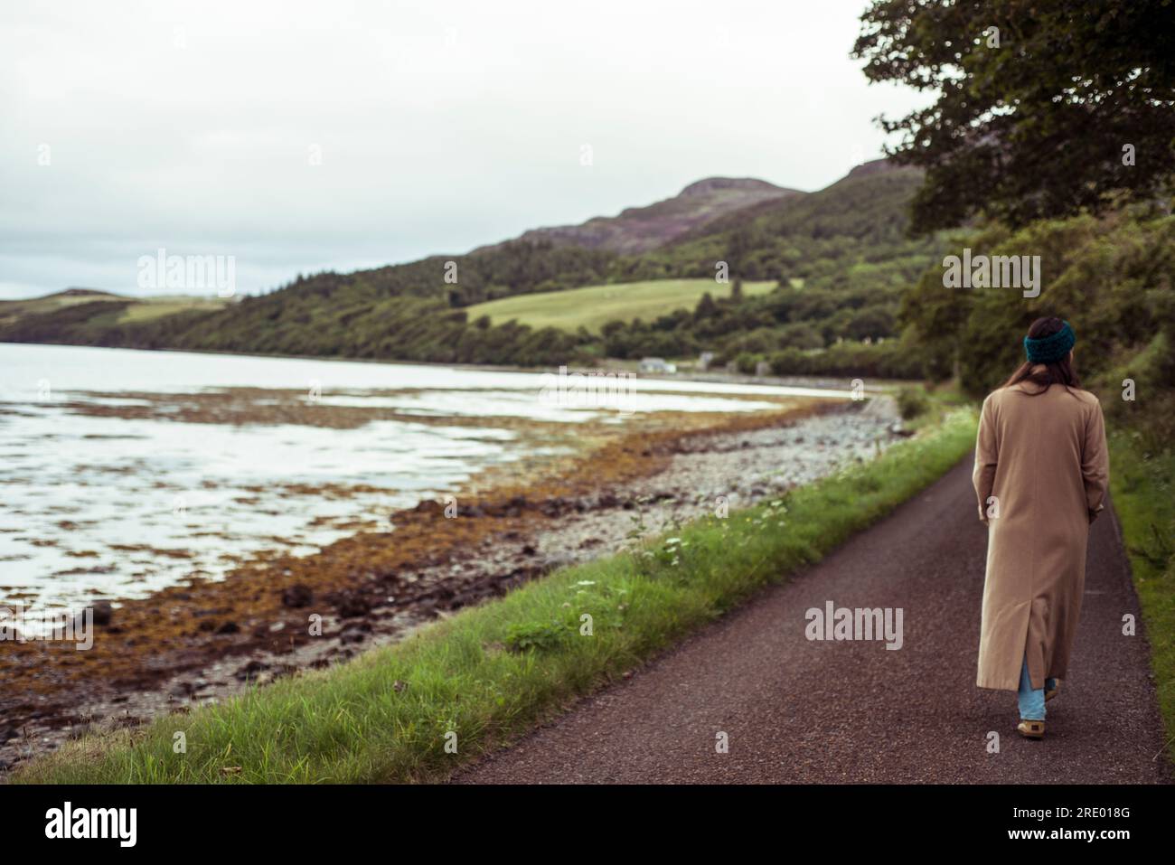 Back view of person walking along small path around lake in mountains ...