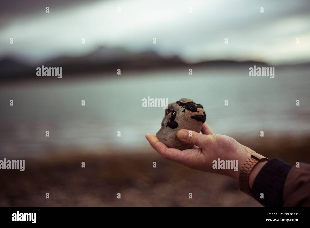 Hand with stone in front of mountain lake Stock Photo - Alamy