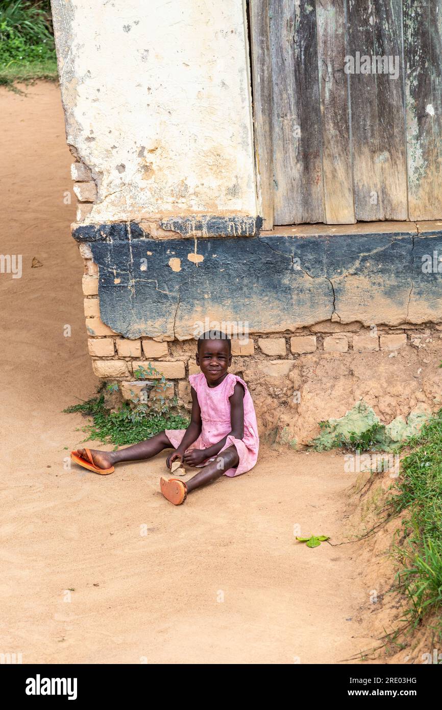 Young girl dressed in pink sitting near a modest dwelling house ...