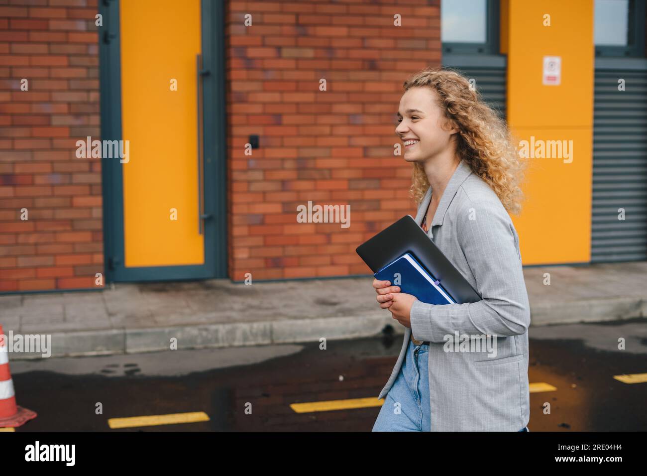 Side view of a student girl with laptop going to the entrance to the ...