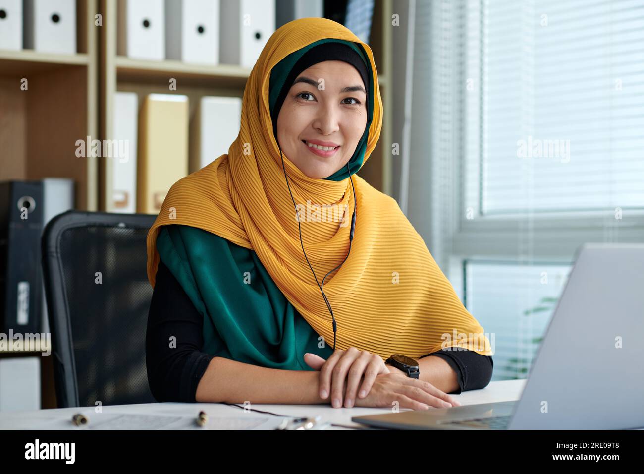 Portrait of smiling muslim entrepreneur in yellow hijab sitting at ...