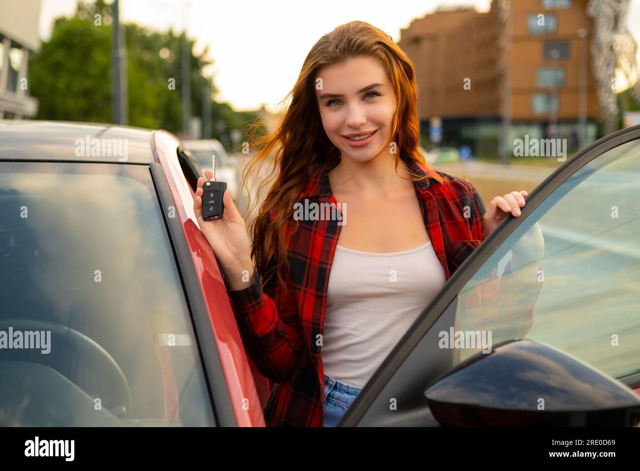 Standing gracefully beside a recently purchased red car, a redhead ...