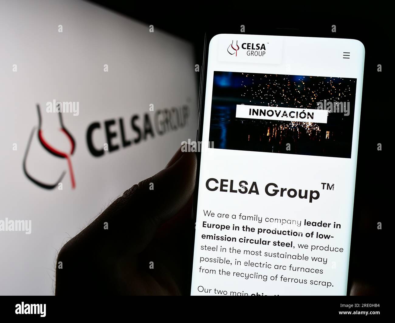 Person holding cellphone with website of Spanish steel company CELSA Group on screen in front of ...
