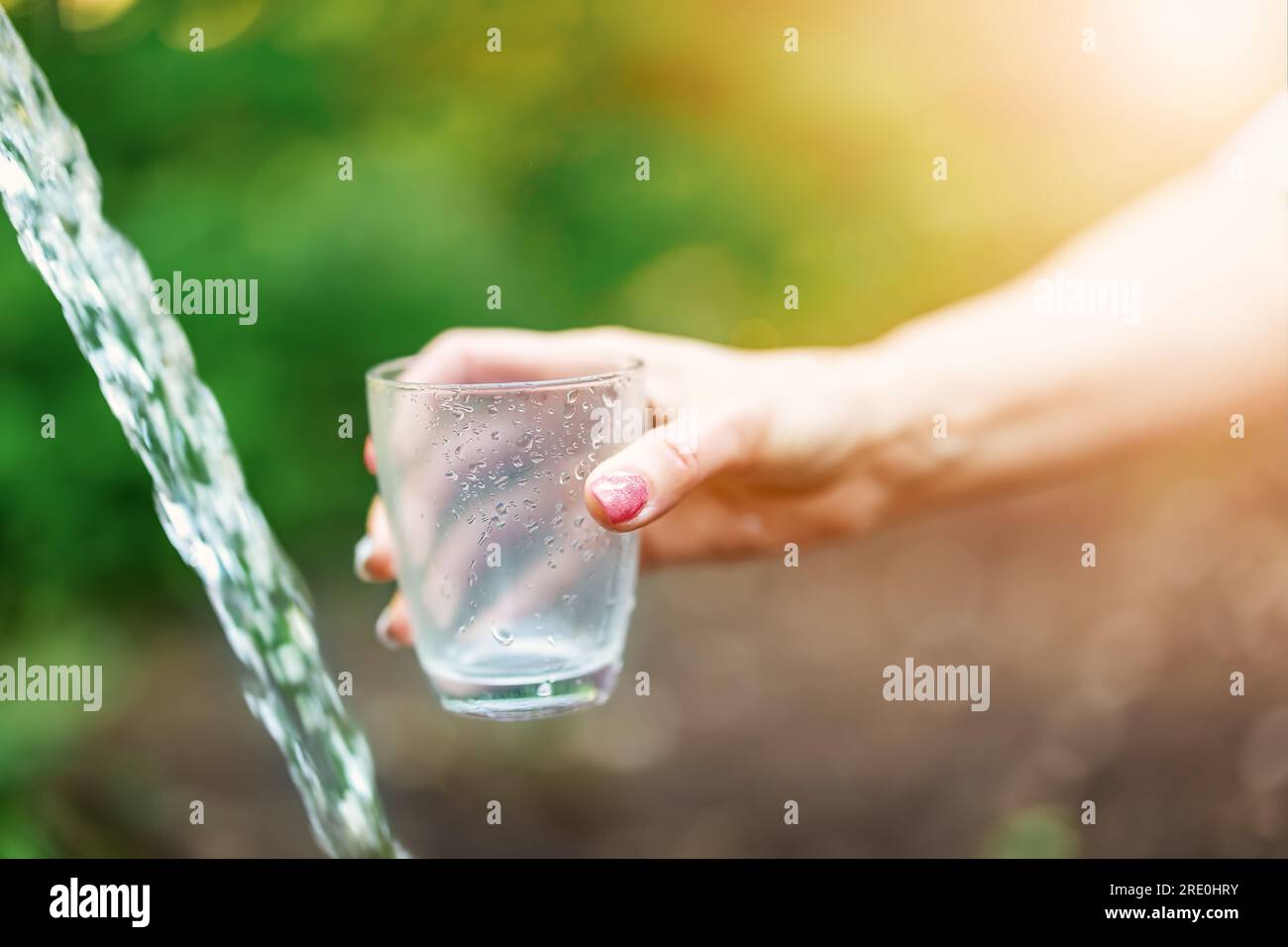 Woman want to pour water from a natural spring into a transparent glass ...
