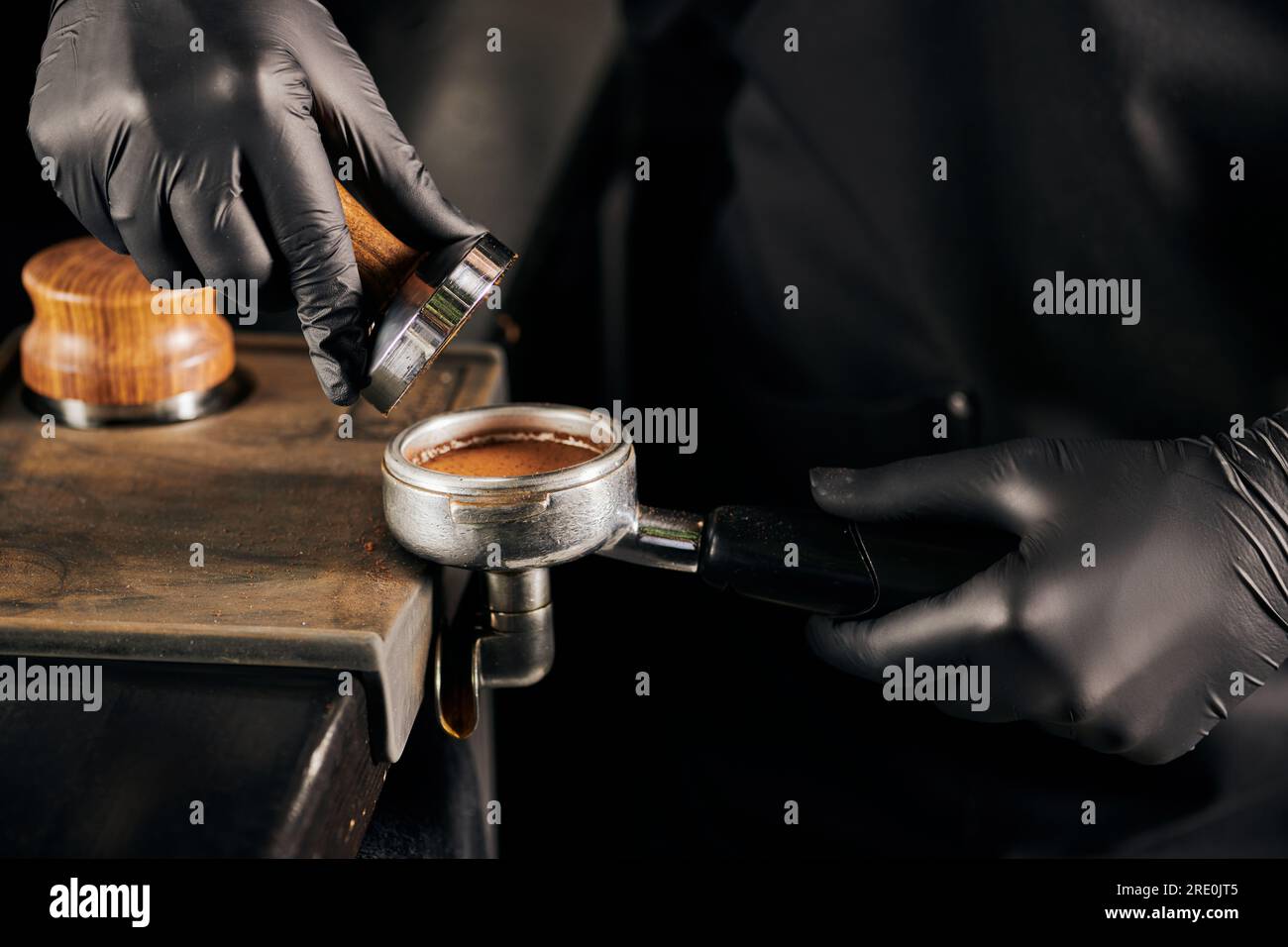 cropped view of barista in black latex gloves pressing ground coffee in ...
