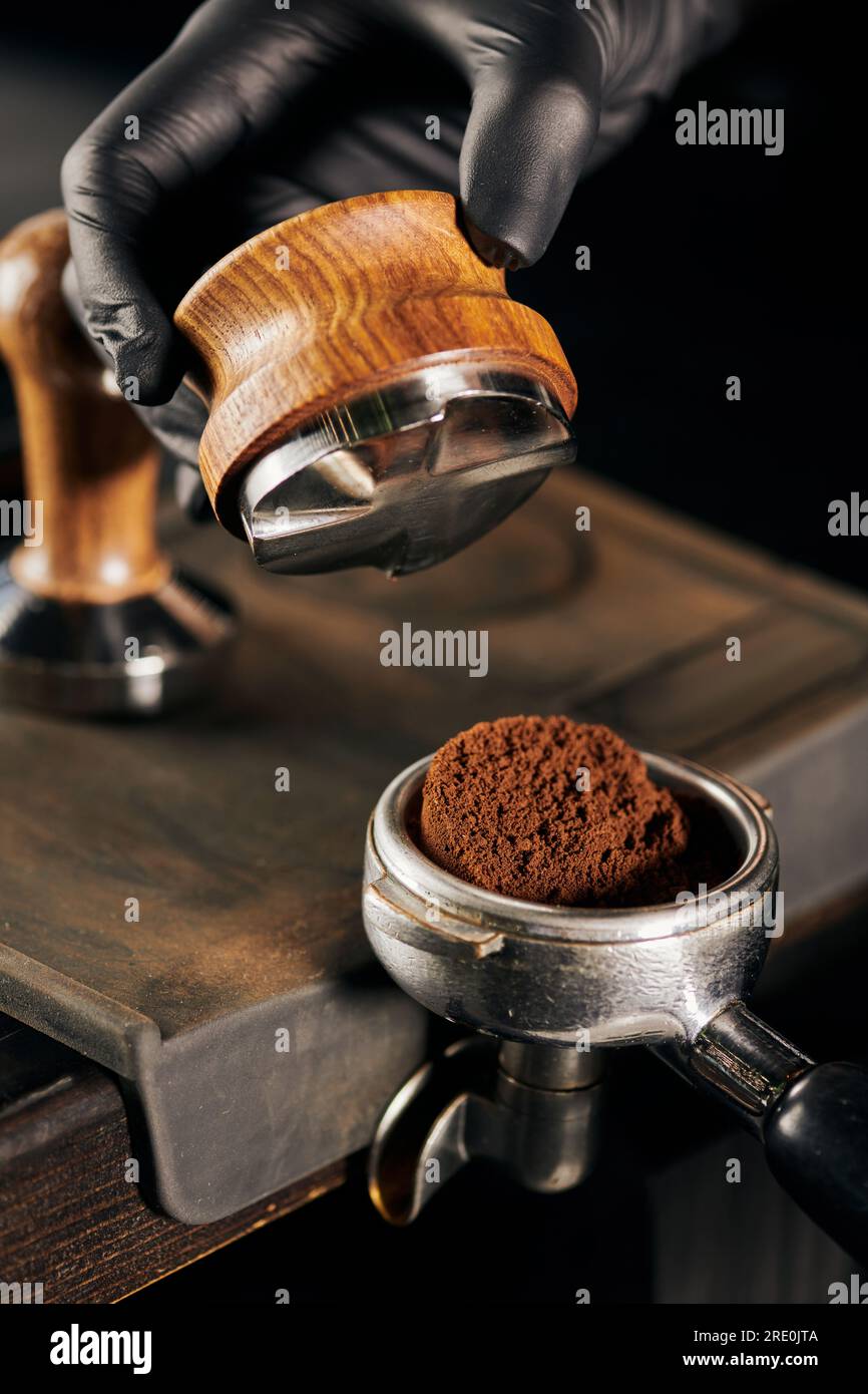 partial view of barista in black latex glove holding tamper near ...