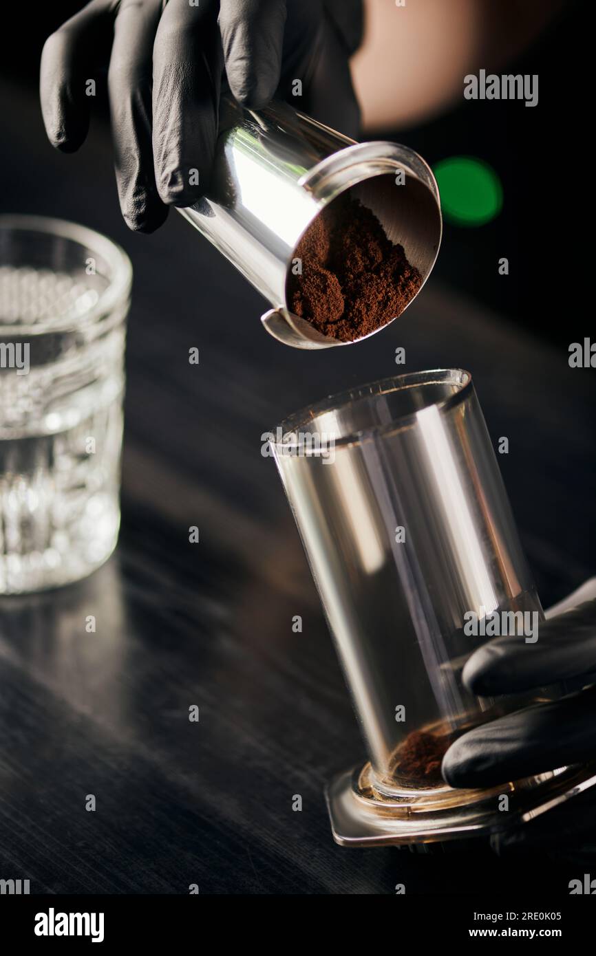 barista in black latex gloves pouring ground coffee in aero press ...
