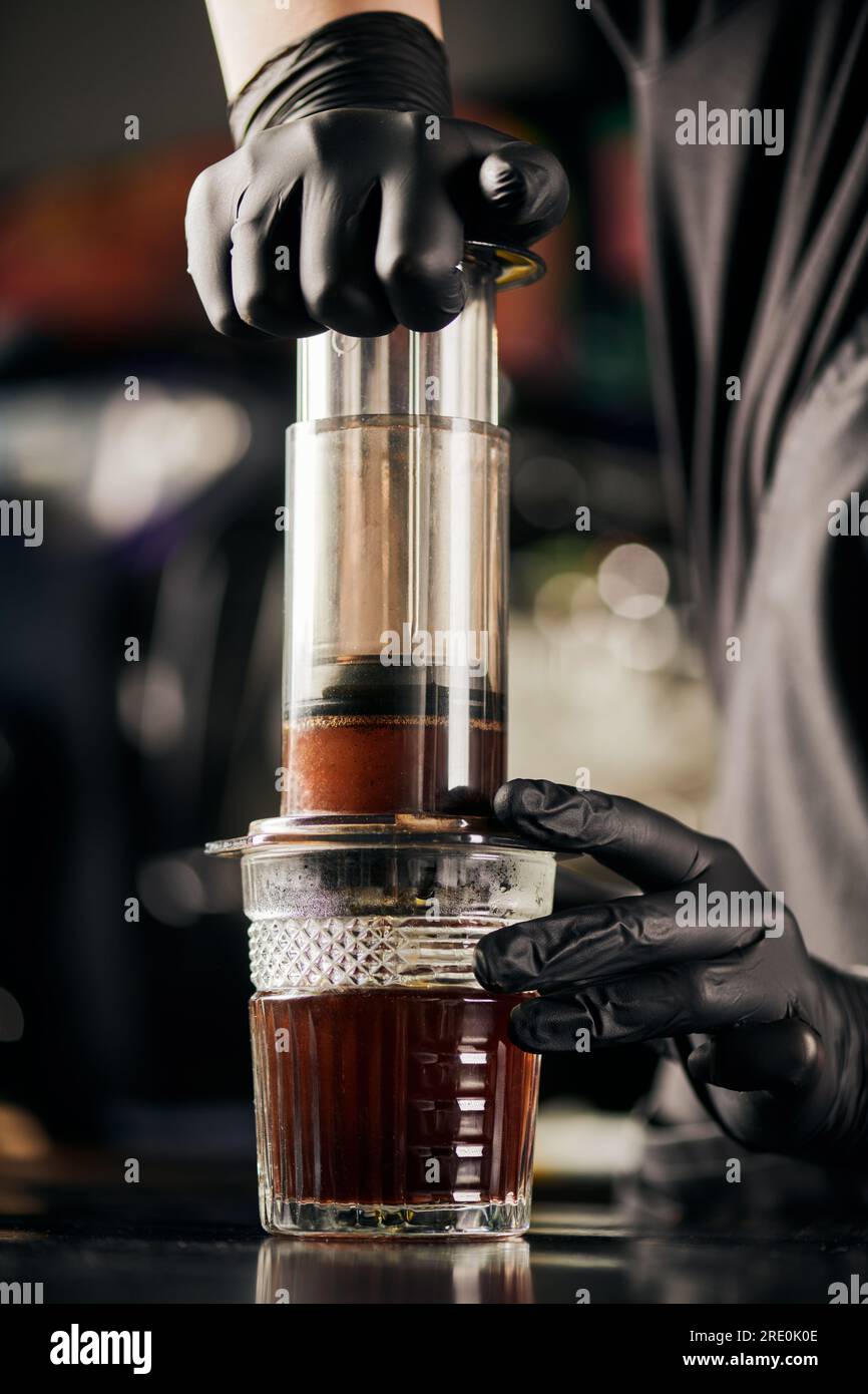 barista in black latex gloves pressing ground coffee in aero press ...