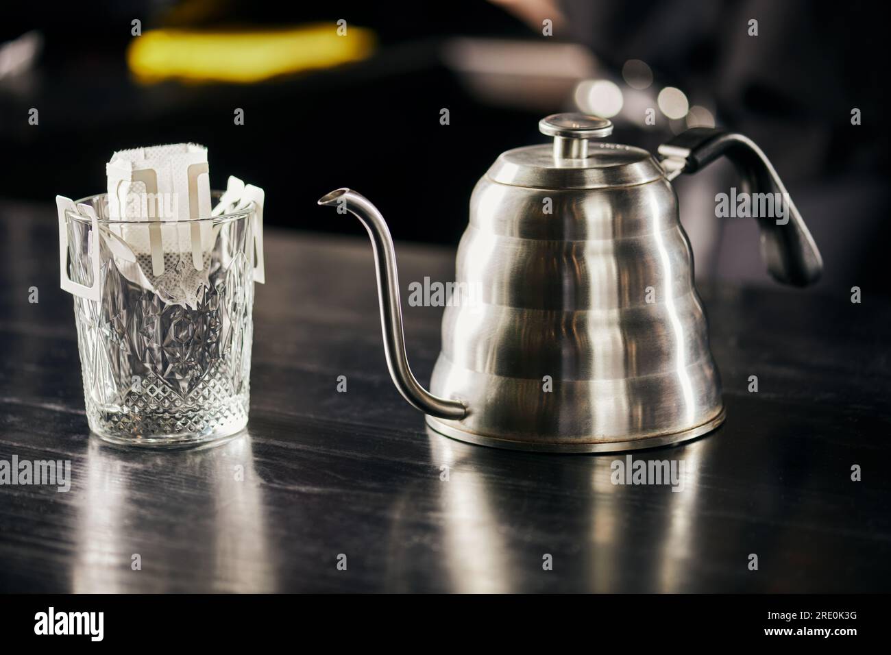 glass with ground coffee in filter bag, metallic drip kettle on black ...