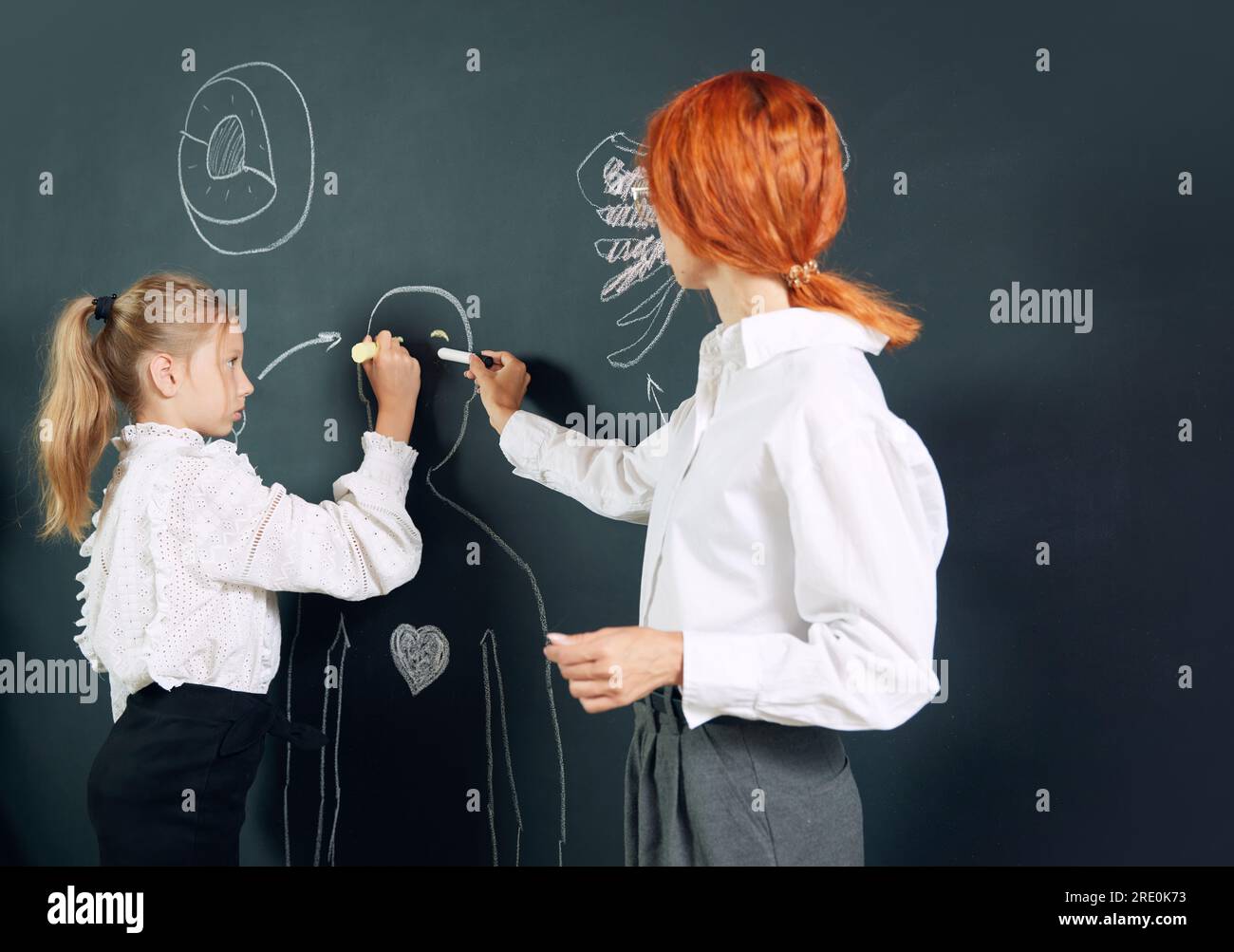 Girl, student of primary school standing at chalkboard with teacher and ...