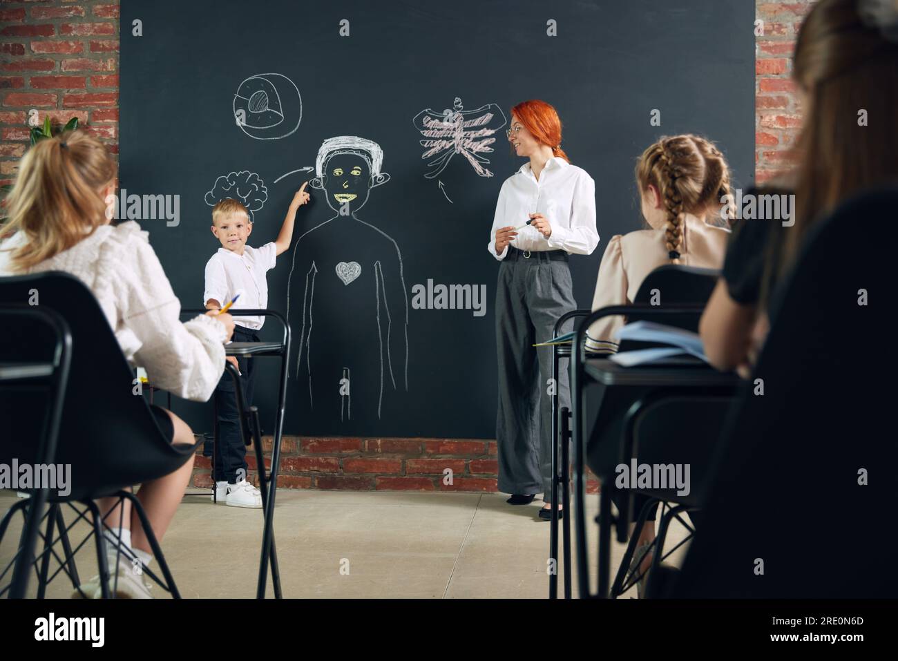 Boy, student of elementary school standing at chalkboard with teacher ...