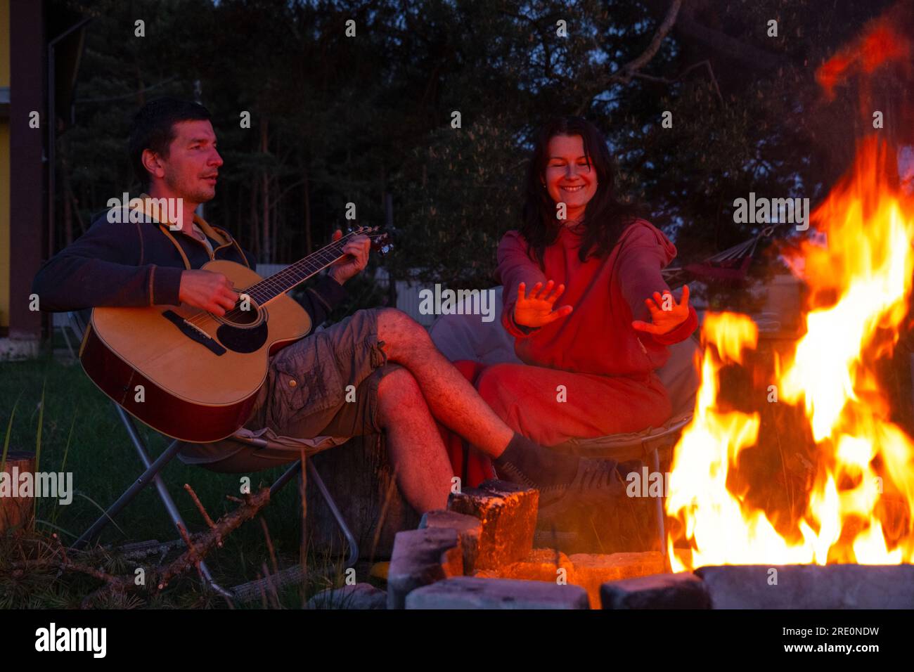 A man plays the guitar, a woman listens and sings along. A couple in love is sitting by the ...