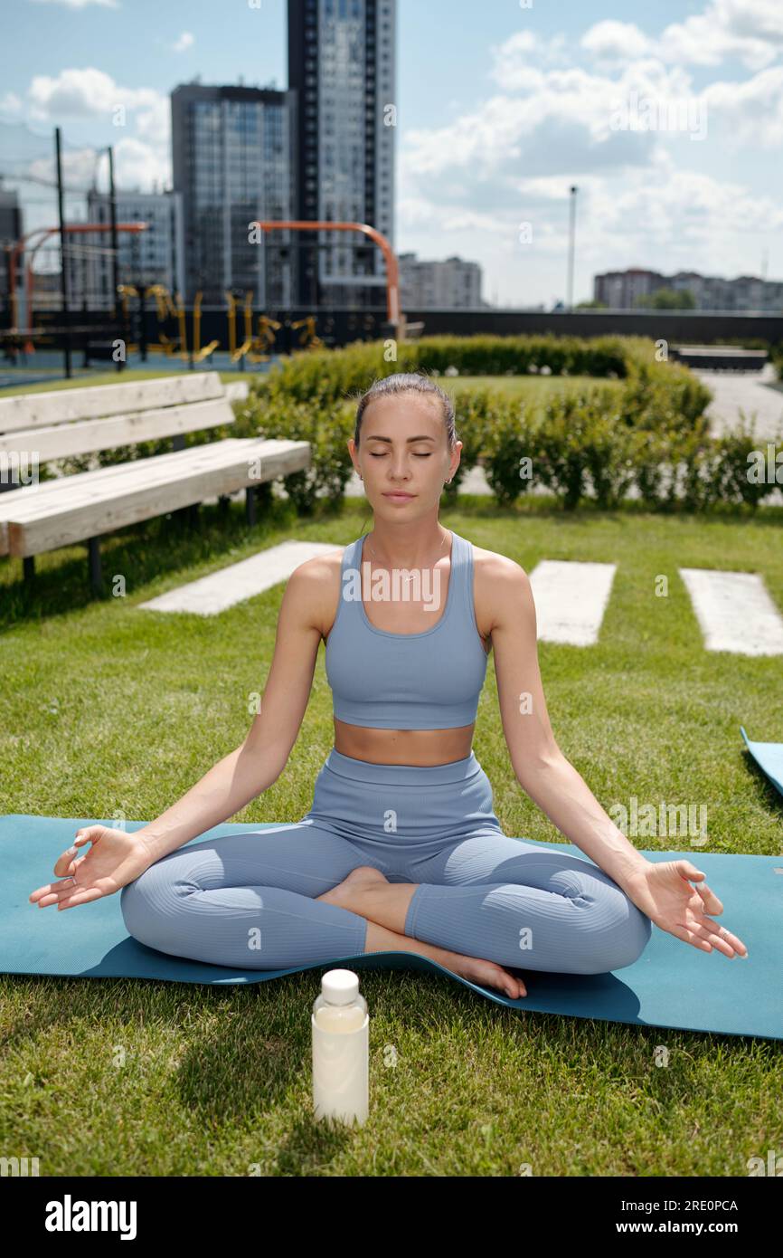 Young serene barefoot woman in tracksuit sitting on mat in pose of ...