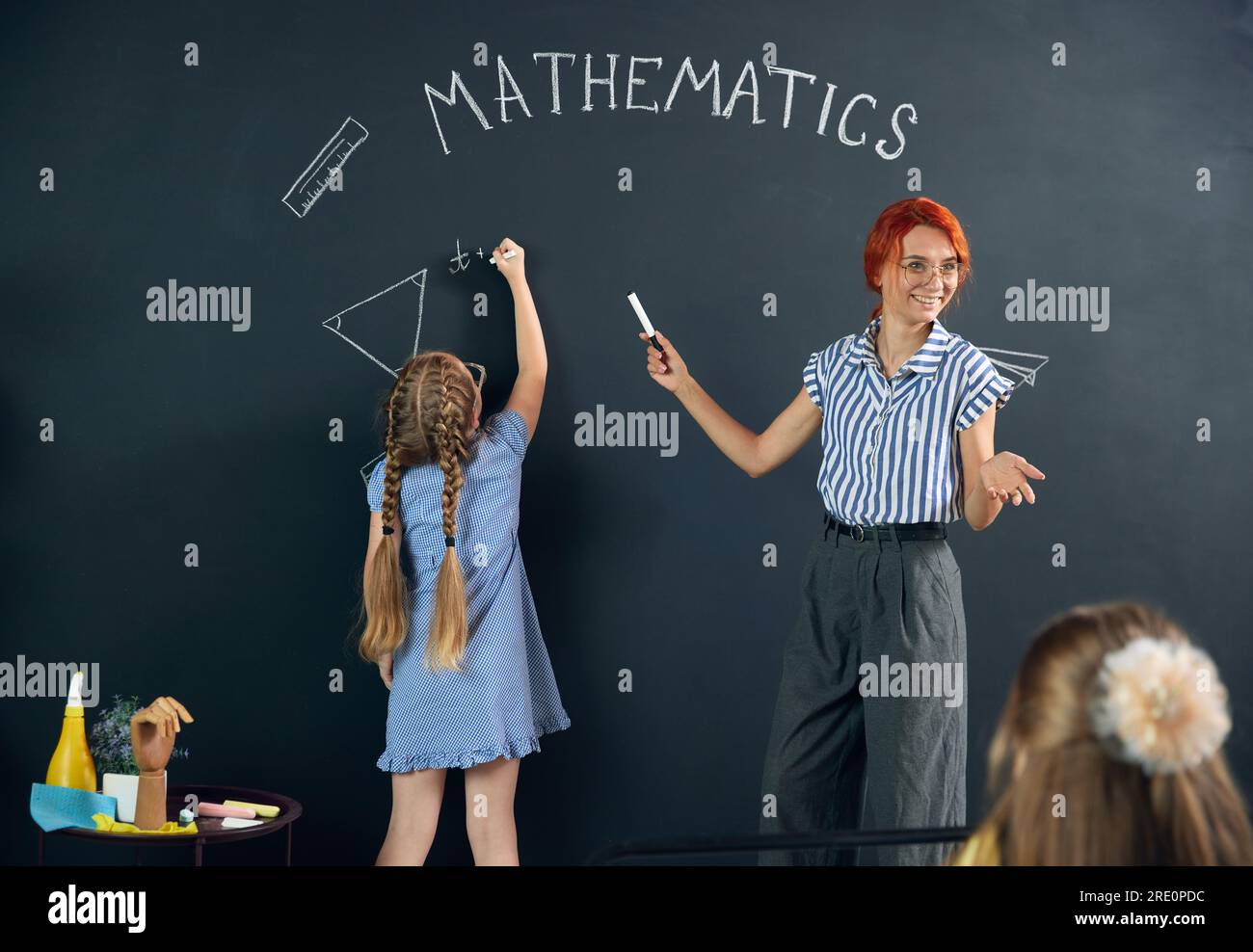 Little girl, child standing at chalkboard, drawing triangle, doing math ...