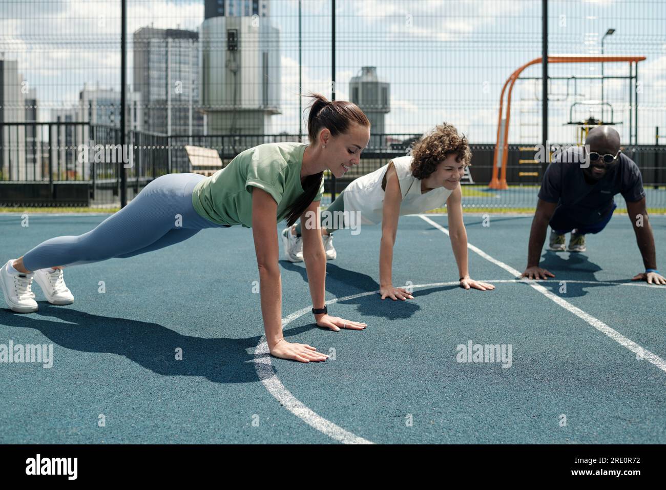 Three happy young intercultural athletes in activewear doing press ups ...