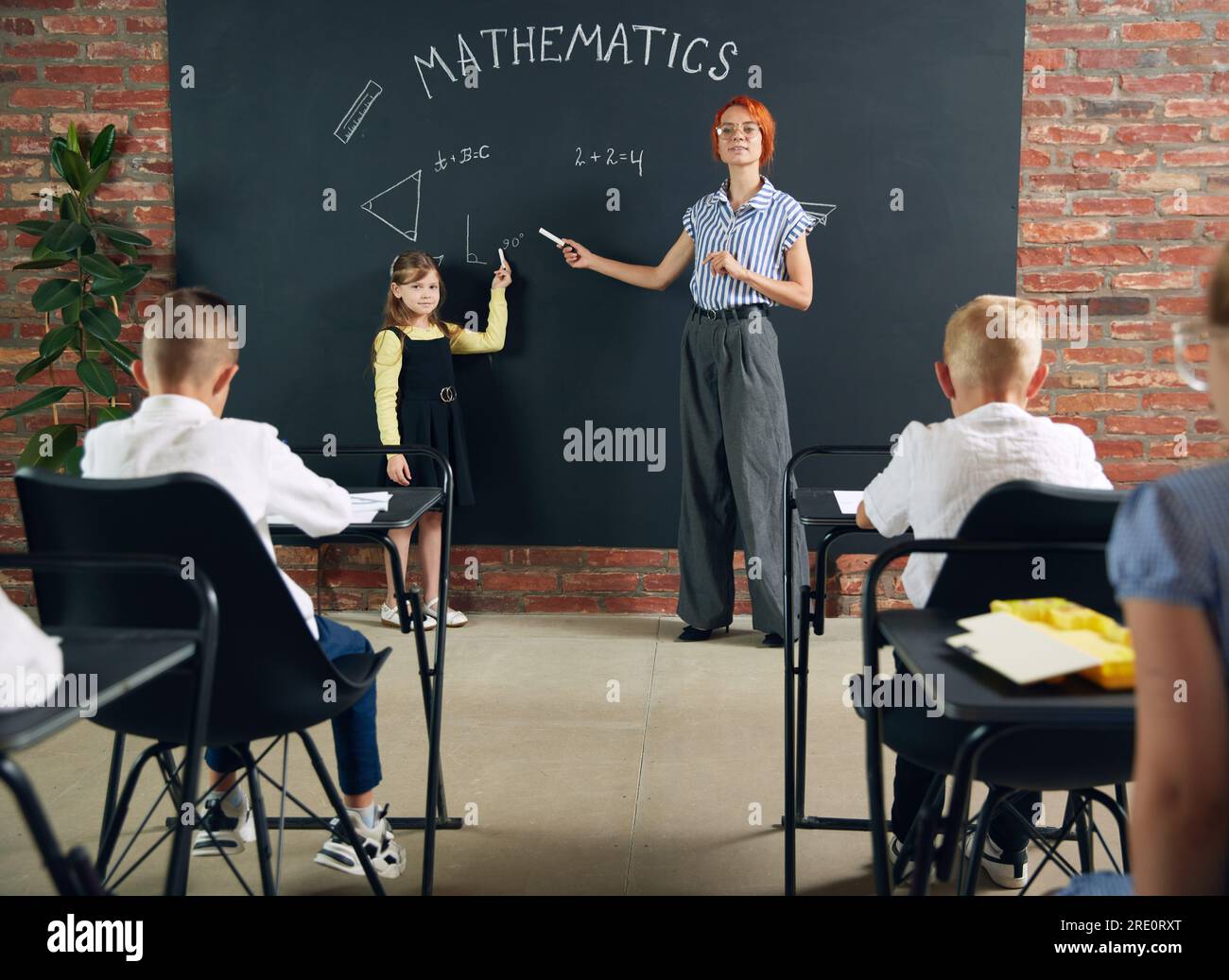 Young woman, teacher standing by blackboard with little girl, child and ...