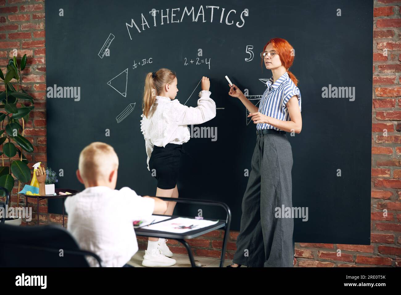 Young woman, teacher of math standing by blackboard with little girl ...
