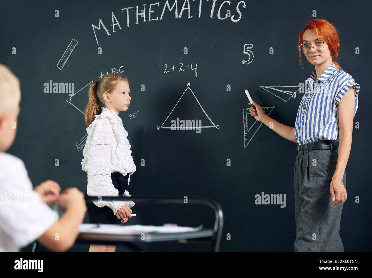 Young woman, teacher of math standing by blackboard with little girl ...