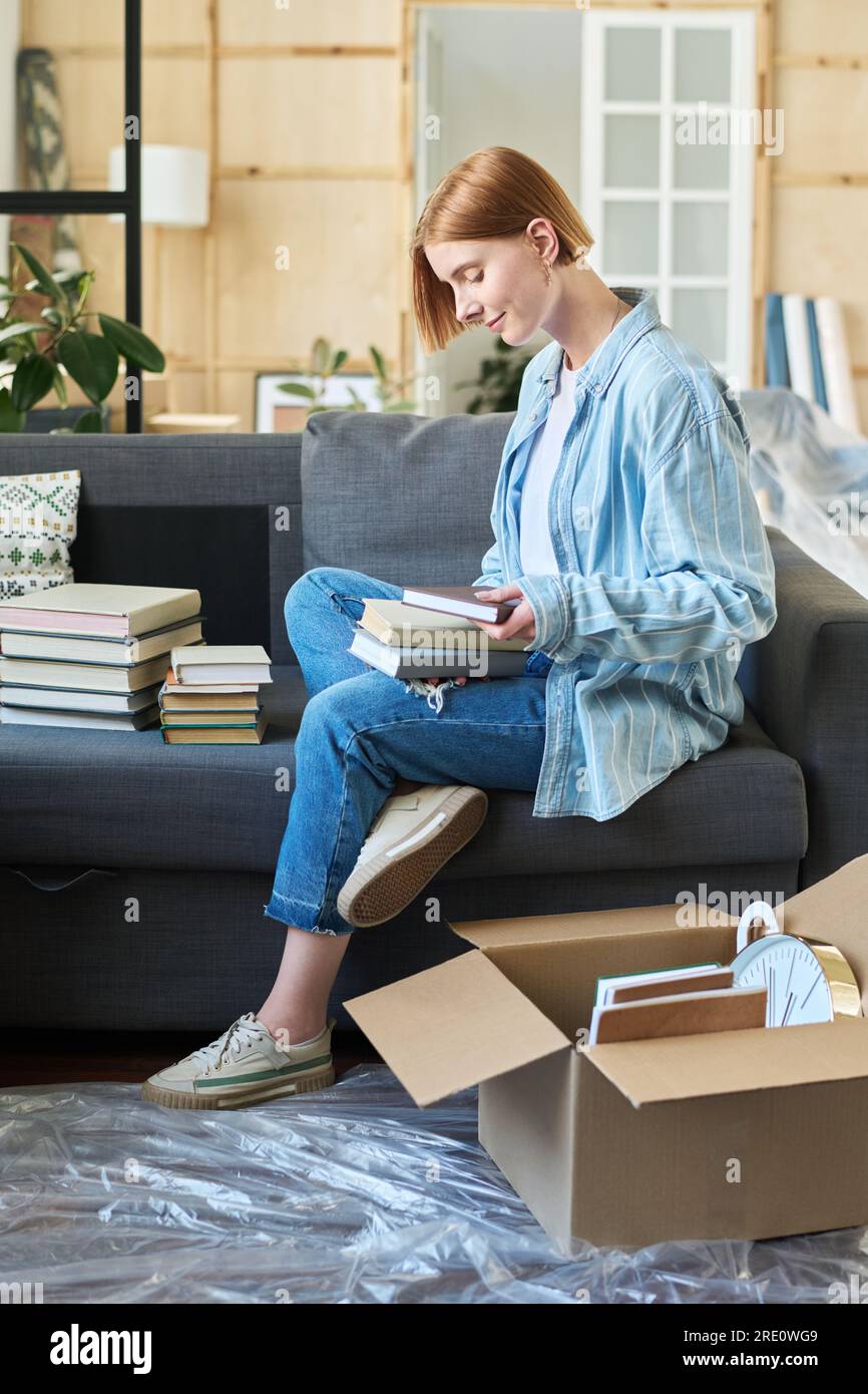 Side view of young female student unpacking cardboard box with books ...
