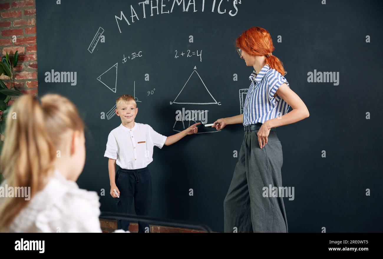 Young woman, teacher standing by blackboard with little boy, child and ...