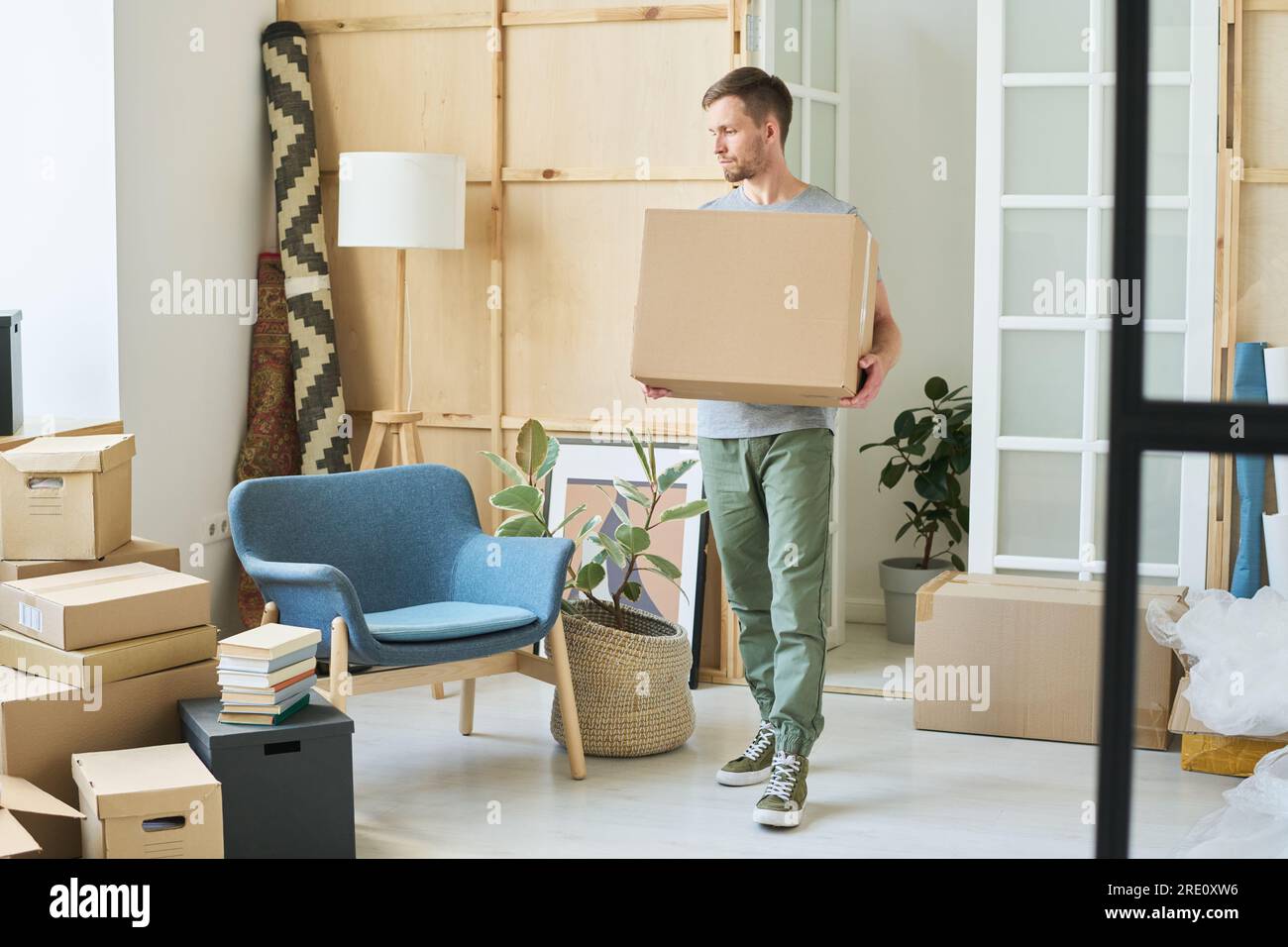 Young male loader carrying big cardboard package while moving along ...